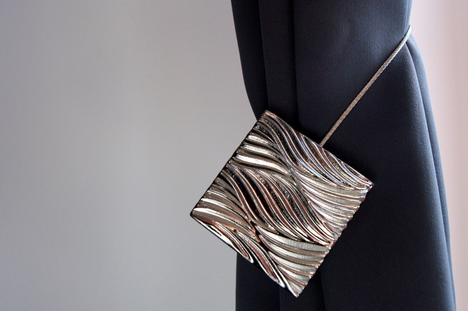 Uma clutch metálica com textura pendurada em uma peça de roupa azul escura.