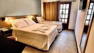 Quarto de hotel com duas camas, uma mesa, uma cadeira, televisão e janela com cortinas.
