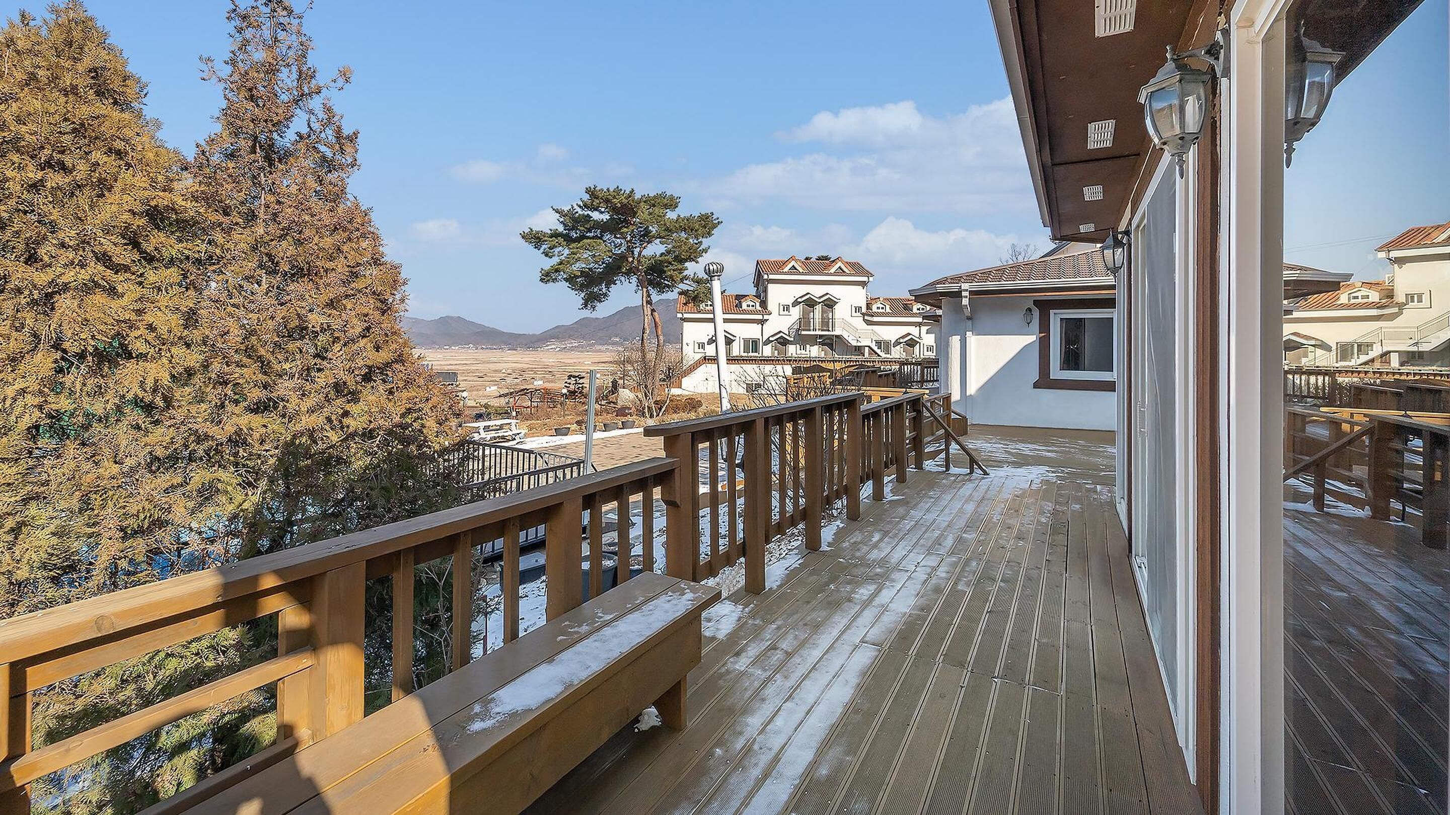Um deck de madeira com um banco, com vista para uma área residencial com casas e uma montanha ao fundo.