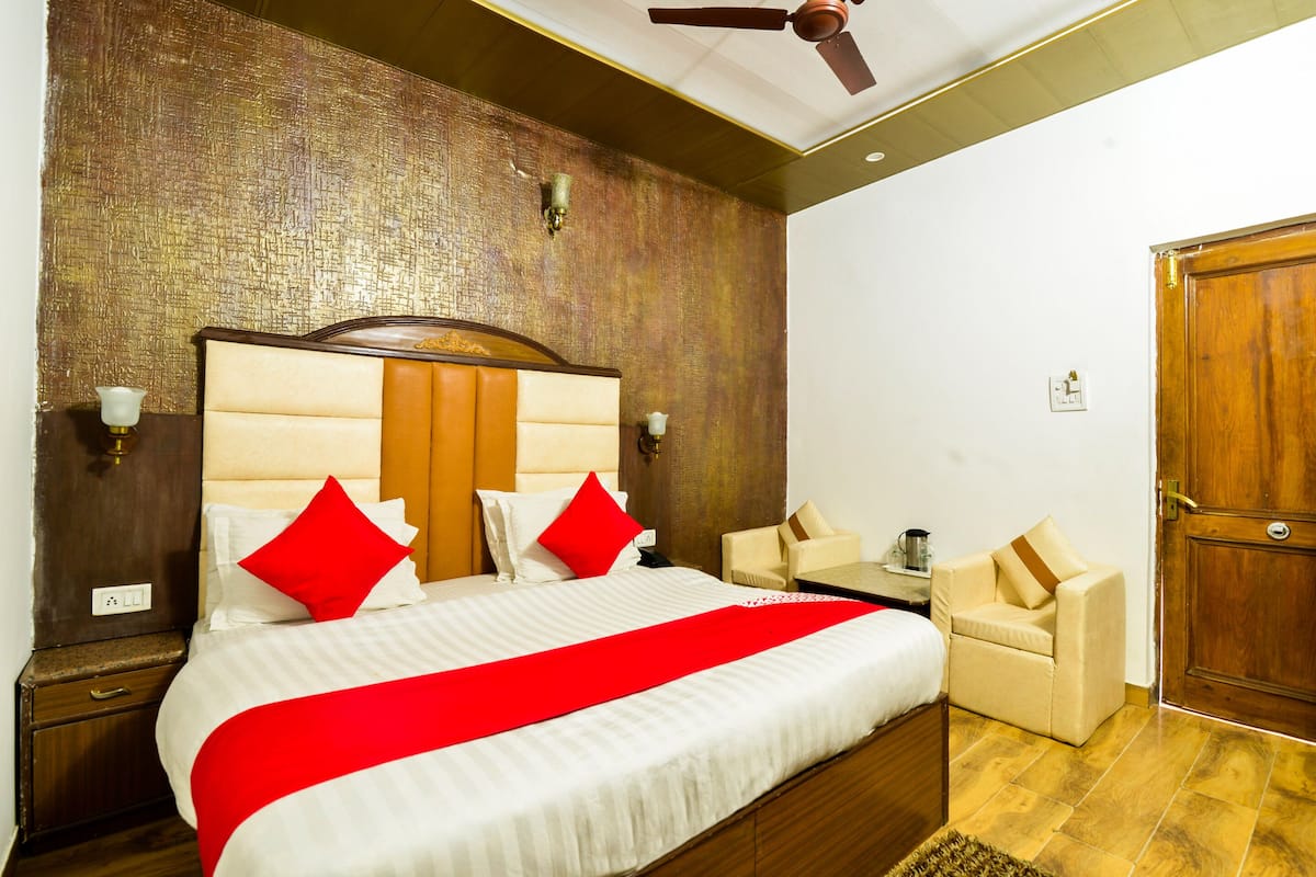 Quarto de hotel com uma cama grande, cabeceira de madeira, duas mesas de cabeceira, um criado-mudo, porta de madeira e ventoinha no teto.