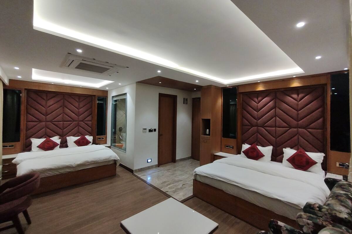 Quarto de hotel moderno com duas camas, um sofá, uma mesinha e um espelho.