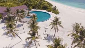 Um resort tropical com piscina, rodeado por palmeiras e uma praia.