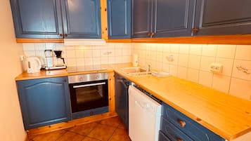 Cozinha compacta com armários azuis, bancada de madeira, forno embutido, máquina de lavar louça e cafeteira.