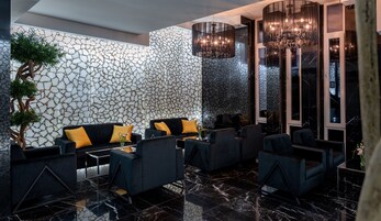 Uma área de estar moderna com parede de pedra, móveis em preto e cinza, e um grande candelabro.