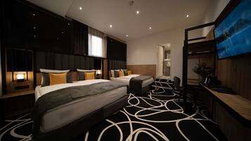 Quarto de hotel com duas camas, uma escrivaninha, televisão e um tapete estampado.