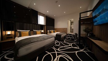 Quarto de hotel com duas camas, uma escrivaninha, televisão e um tapete estampado.