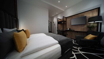 Quarto de hotel moderno com uma cama grande, uma mesa de escritório, uma cadeira e uma televisão de tela plana na parede.
