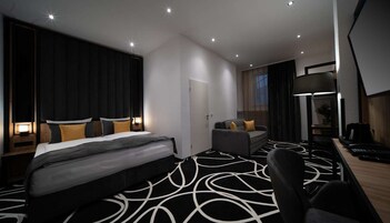 Quarto de hotel moderno com uma cama grande, uma escrivaninha, uma cadeira e um sofá.