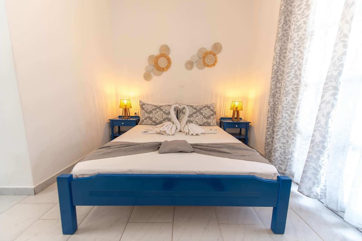 Uma cama bem arrumada com estrutura azul, duas luminárias de cabeceira e arte decorativa na parede.