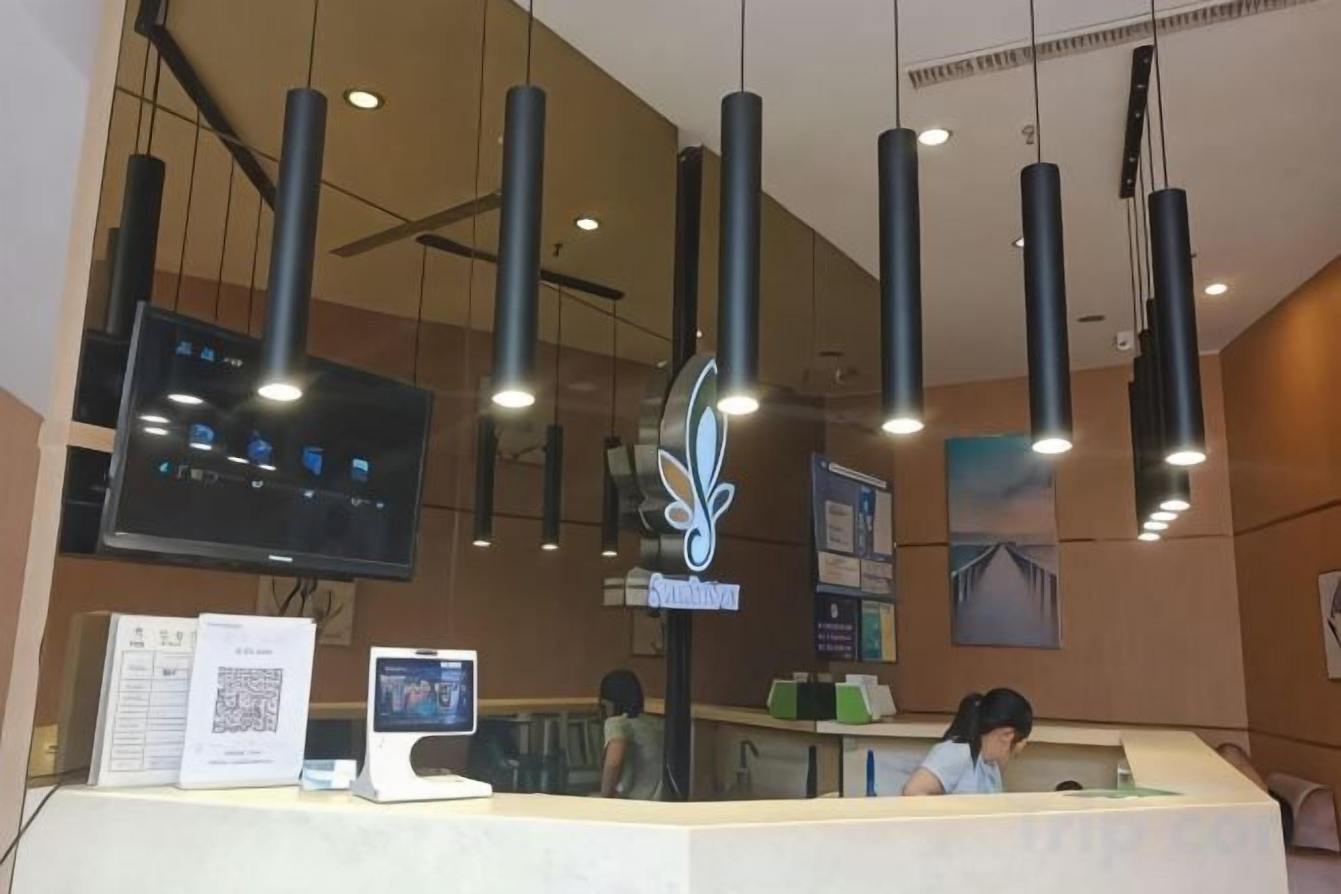 Uma área de recepção com tela digital, balcão e luminárias pendentes.