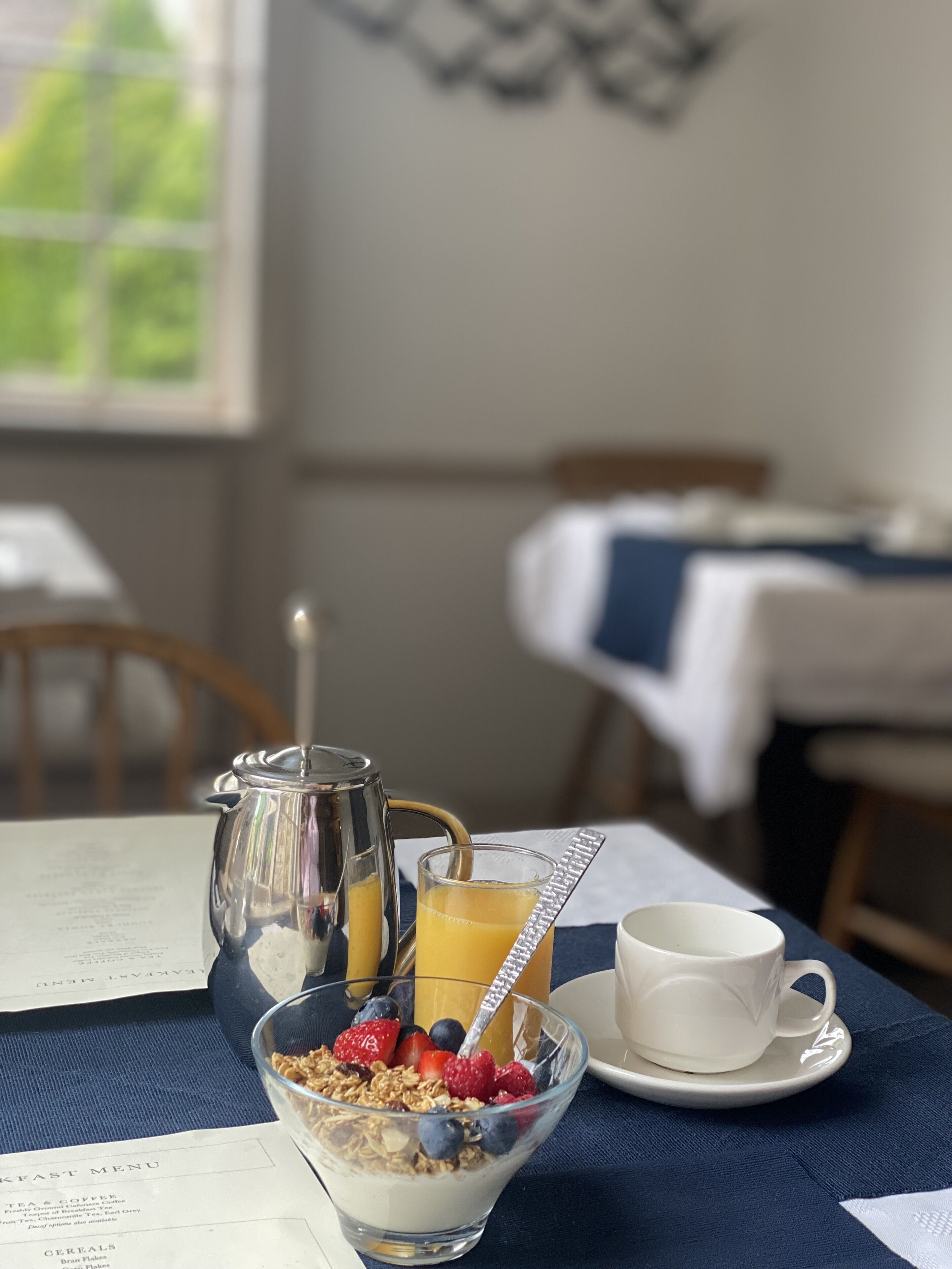 Uma mesa posta para o café da manhã, com uma tigela de cereal coberta de frutas vermelhas, um copo de suco de laranja e uma xícara de café.