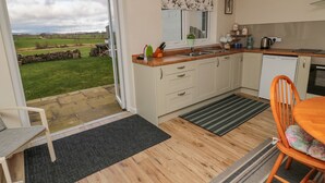 Cozinha moderna com uma janela ampla, área de refeições com mesa e cadeiras, e vista para um campo gramado.