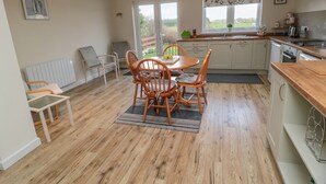 Cozinha moderna com piso de madeira, área de refeições com mesa e cadeiras, e vista pela janela.