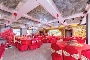 Uma sala de banquetes com mesas redondas e cadeiras, um palco com uma tela grande e decoração vermelha.