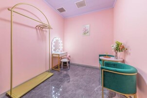 Um quarto em tons de rosa com uma toucador, um espelho iluminado, uma cadeira e outra verde.