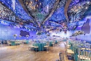 Uma sala de banquetes com mesas redondas, cadeiras e um candelabro.