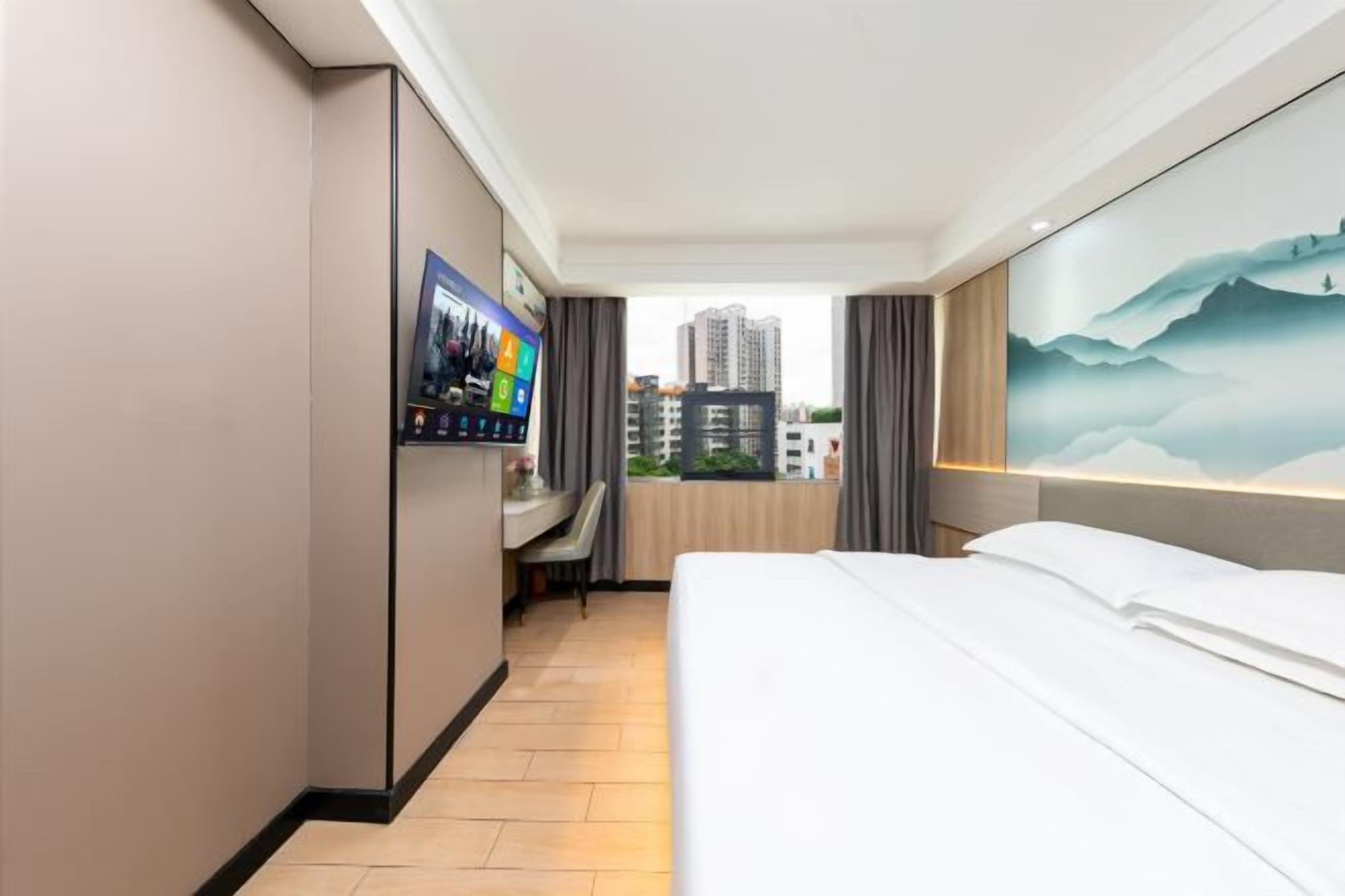 Quarto de hotel com cama, escrivaninha, televisão e vista para a cidade.