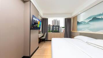 Quarto de hotel com cama, escrivaninha, televisão e vista para a cidade.