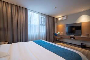 Quarto de hotel com uma cama grande, uma escrivaninha com cadeira, televisão e janela com cortinas.