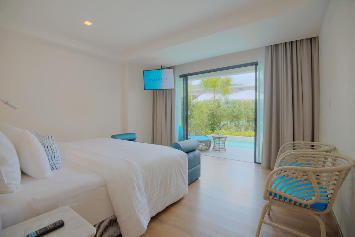 Quarto de hotel com cama, televisão, varanda e uma cadeira com vista.