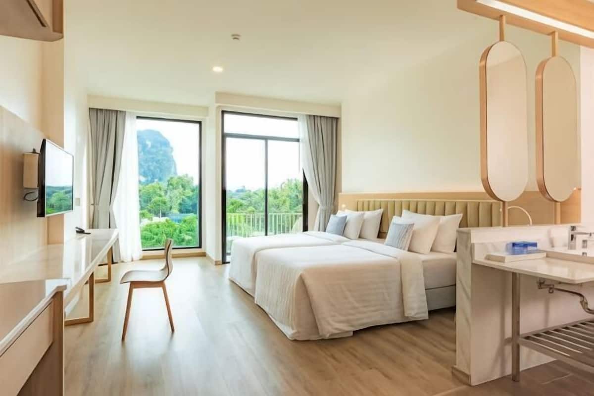 Quarto de hotel com cama, escrivaninha, cadeira, televisão e banheiro.