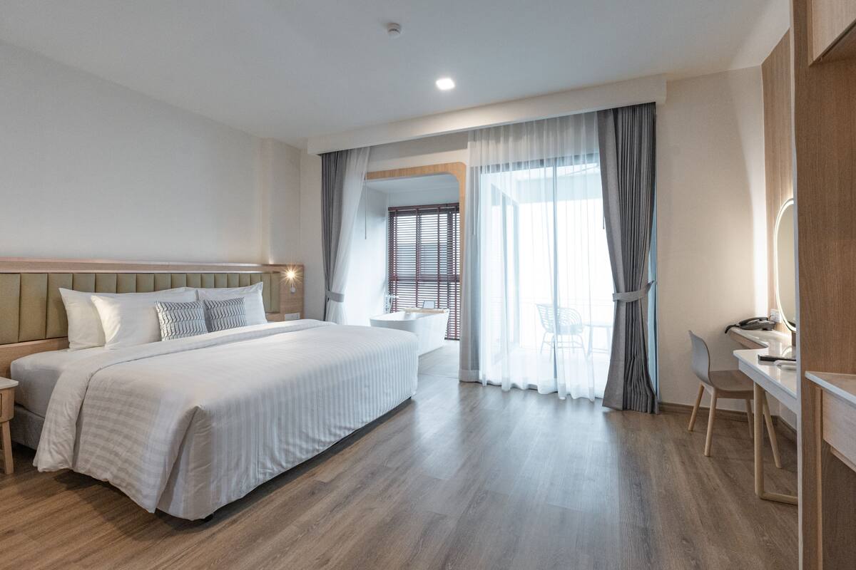 Quarto de hotel moderno com uma cama grande, uma escrivaninha com cadeira e uma janela com cortinas.