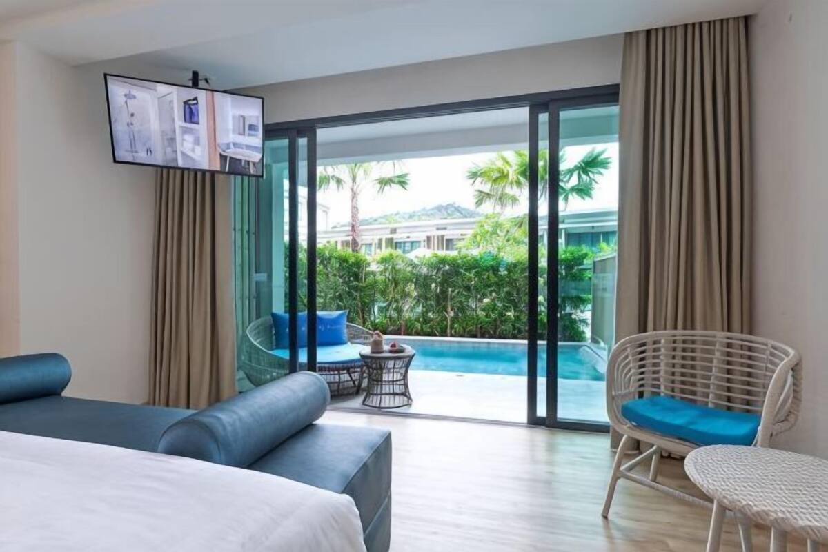 Quarto de hotel com cama, televisão, varanda com piscina e área de estar ao ar livre.