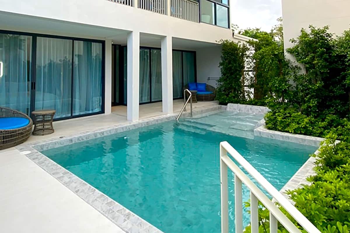 Uma área de piscina moderna com piscina azul cristalina, cadeiras de lounge de vime com almofadas azuis e uma varanda envidraçada.