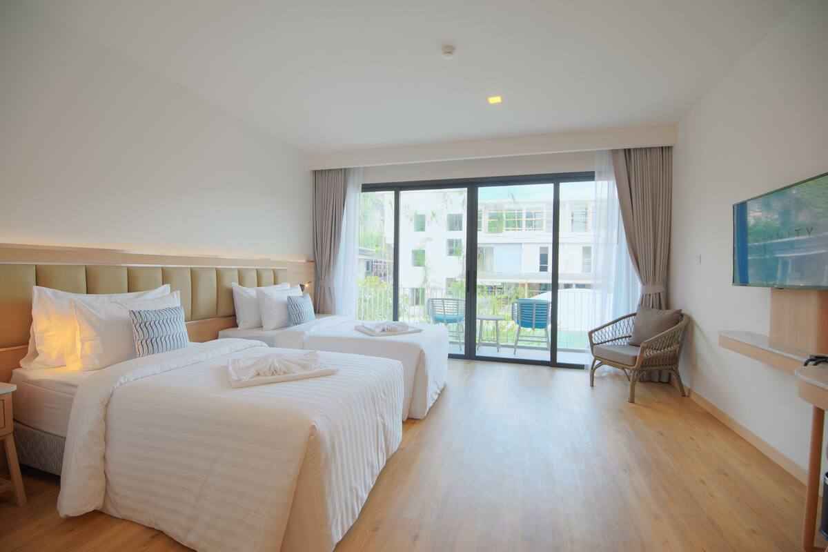 Quarto de hotel com duas camas, uma cadeira e varanda com vista para edifícios.