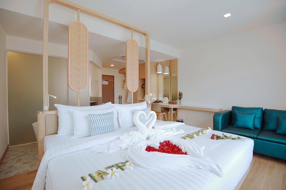 Quarto de hotel com uma cama grande, um sofá verde-água, uma escrivaninha e um espelho.