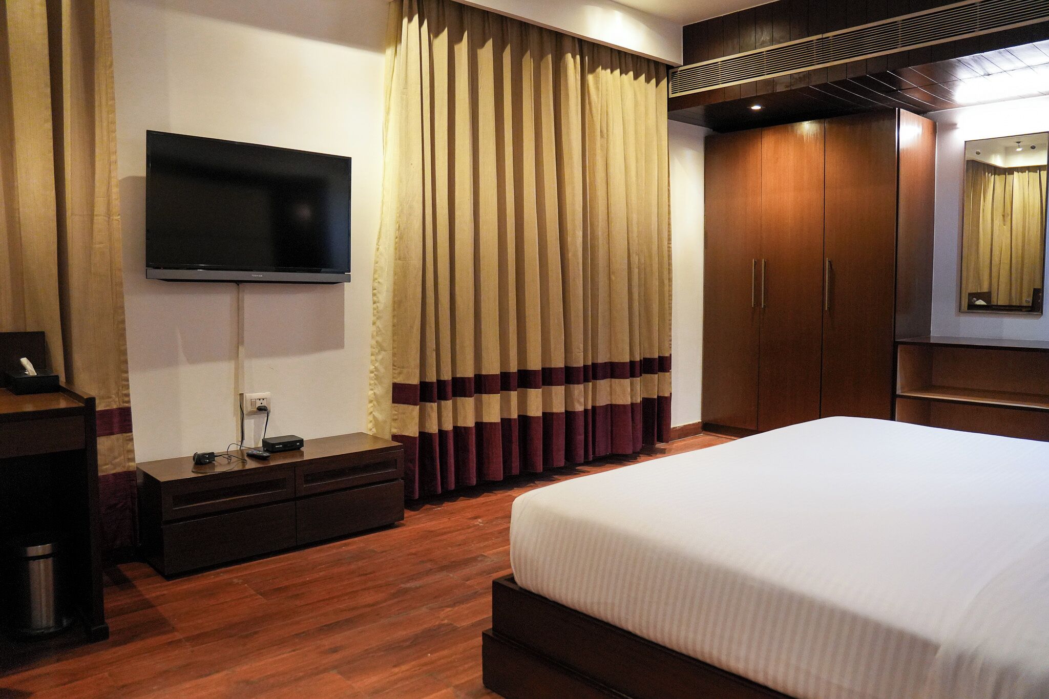Quarto de hotel com cama, televisão na parede, guarda-roupa e espelho.