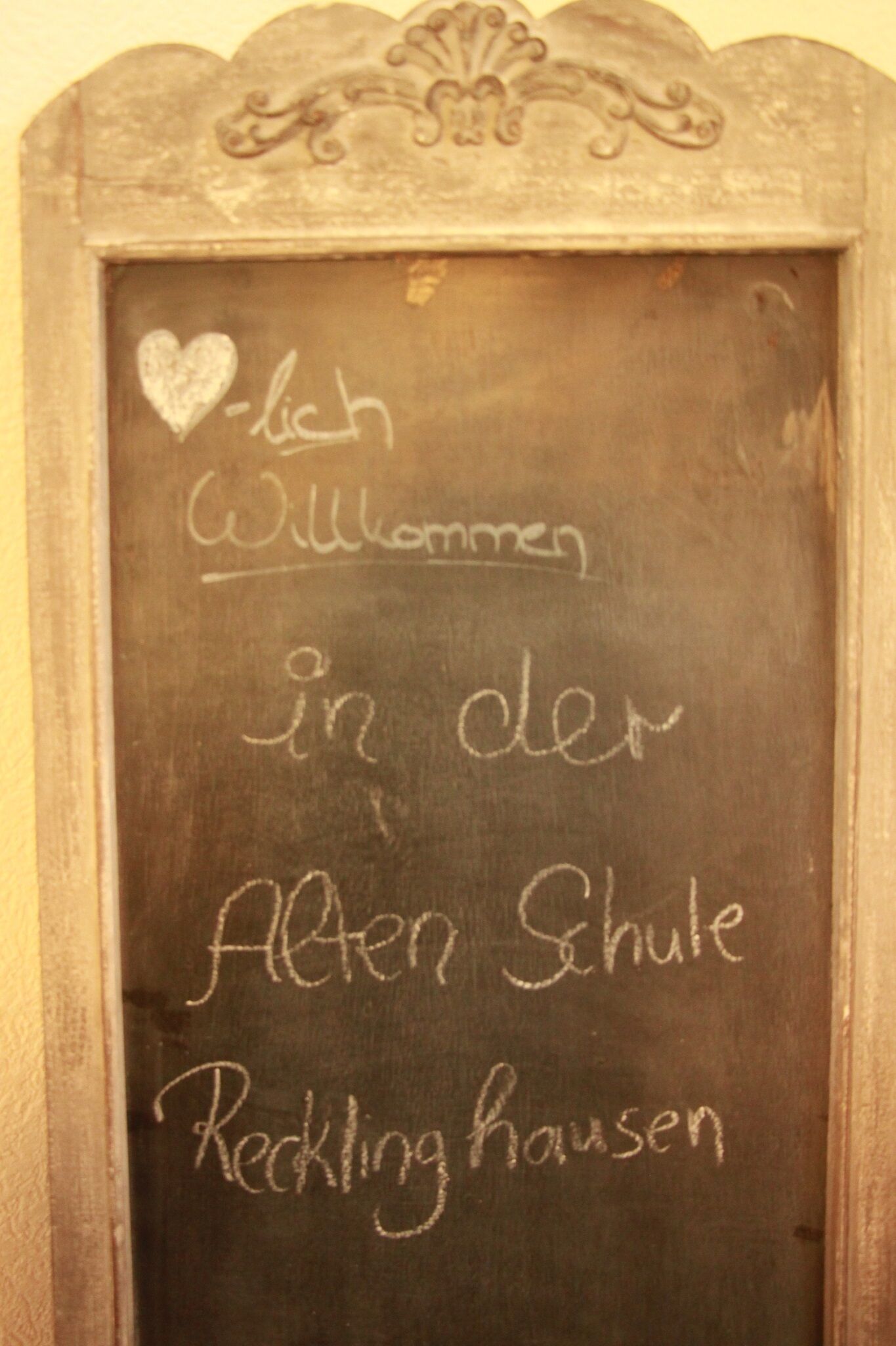 Um quadro negro com a mensagem 'Willkommen in der Alten Schule Recklinghausen' escrita nele.