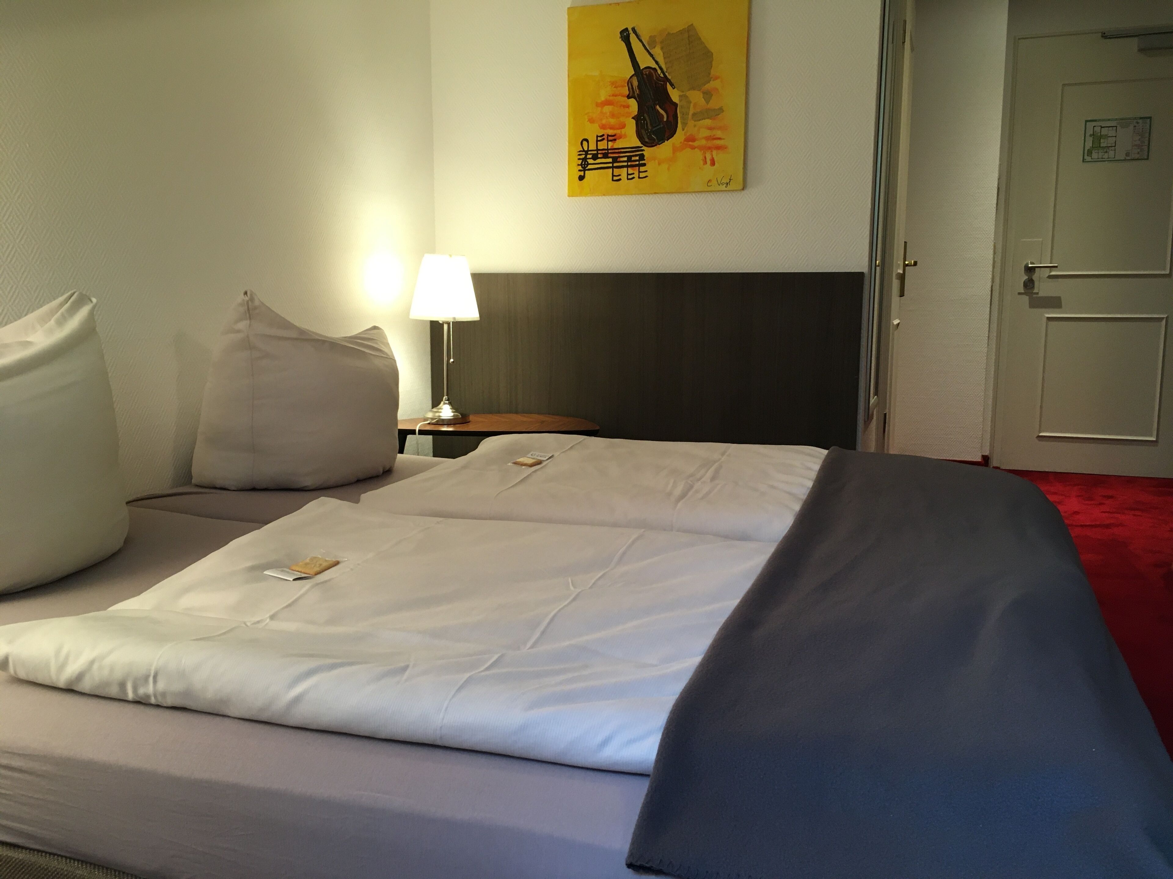 Quarto de hotel com cama bem arrumada, luminária na mesa de cabeceira e um quadro na parede.