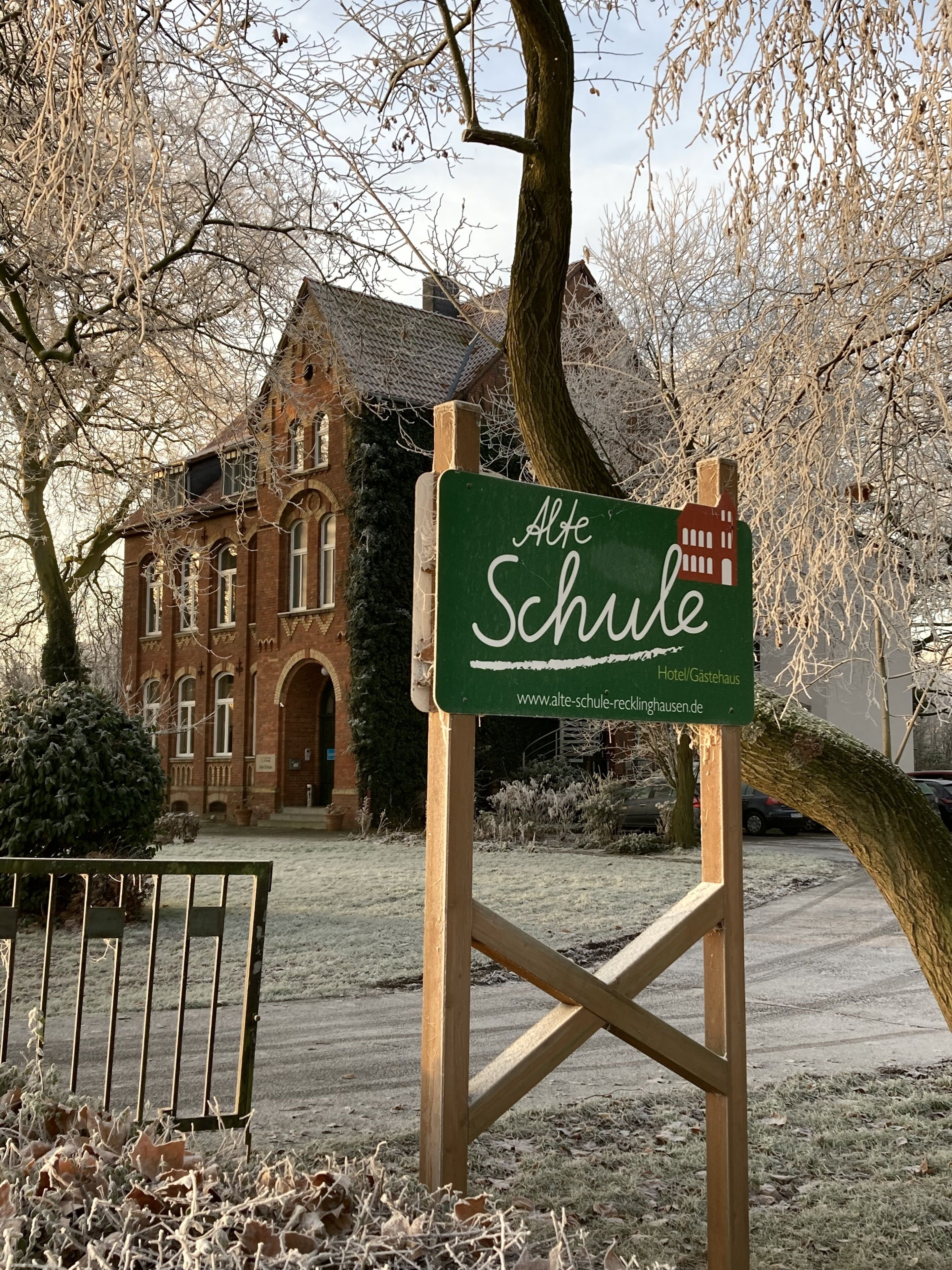 Placa para a Alte Schule, um hotel e pensão, com um edifício histórico ao fundo.