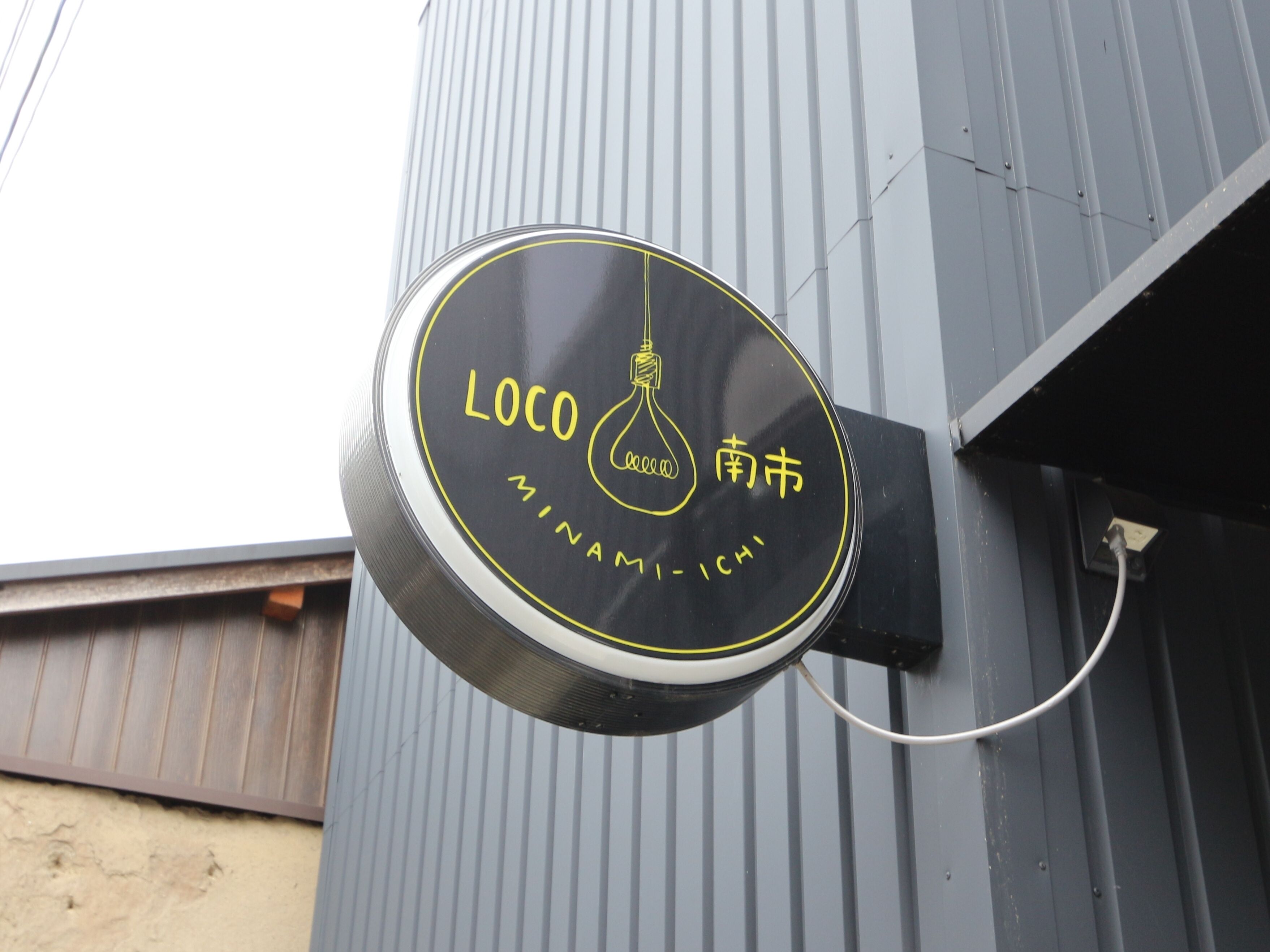 Sinal circular com os textos 'LOCO' e 'MINAMI-CHICHI' em um edifício.