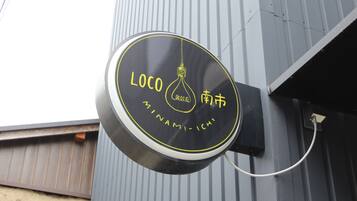 Sinal circular com os textos 'LOCO' e 'MINAMI-CHICHI' em um edifício.