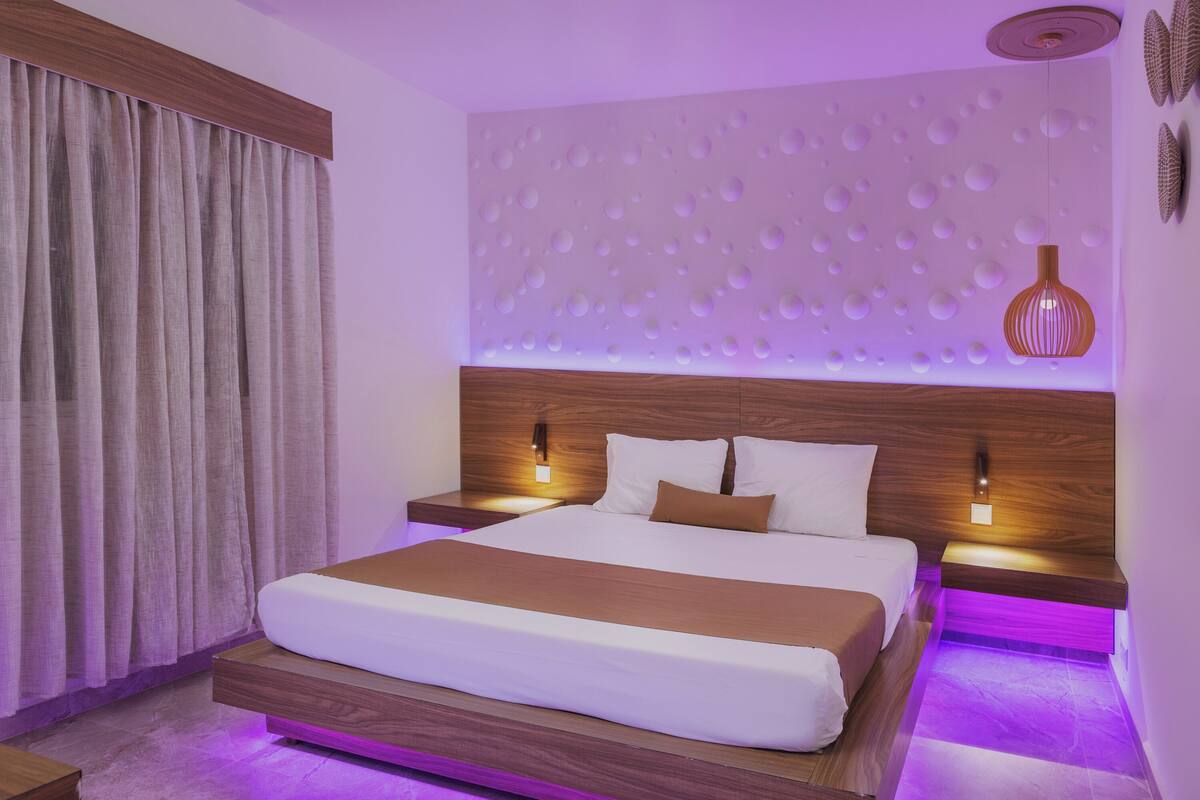Quarto moderno com cama grande, cabeceira de madeira e iluminação ambiente.