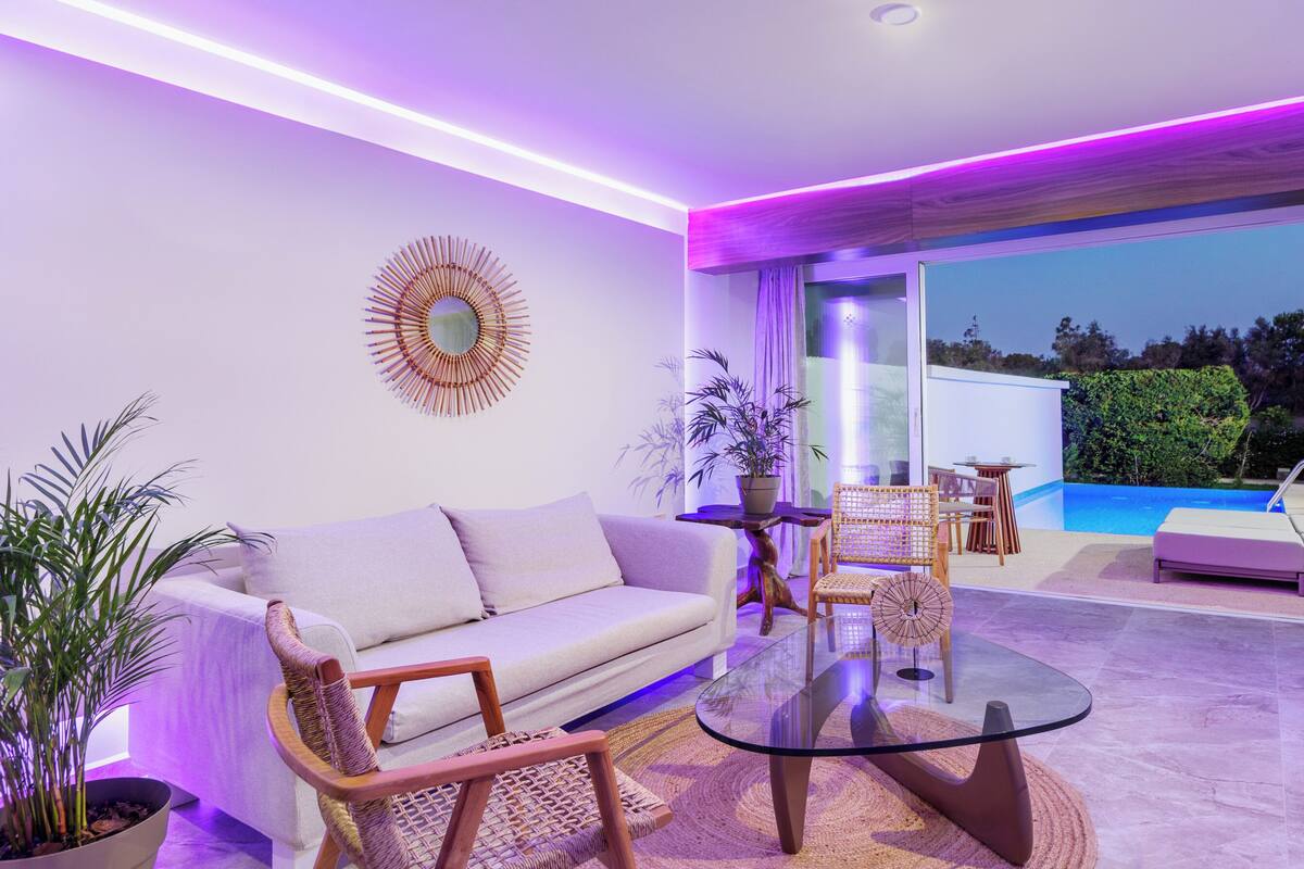 Uma sala de estar moderna com mesa de centro de vidro, móveis de vime, sofá branco e vista para uma piscina.