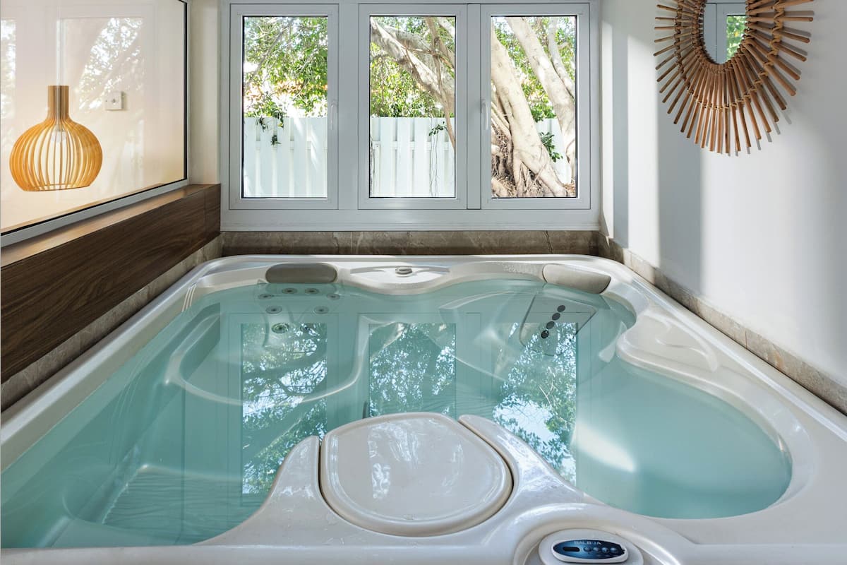 Um spa moderno com banheira de hidromassagem, janelas amplas e um espelho decorativo.