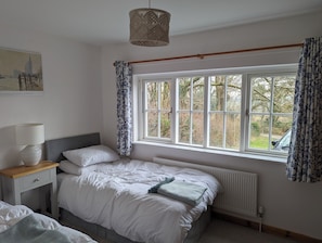 Quarto com cama, mesa de cabeceira, luminária, radiador e janela com cortinas.