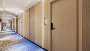 Corredor de hotel com portas, piso coberto por carpete e luminária na parede.