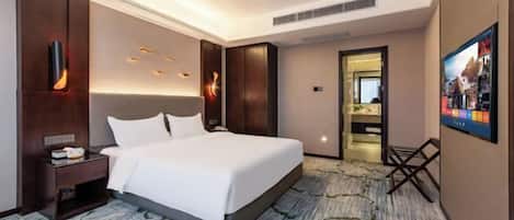 Quarto de hotel com uma cama grande, mesa de cabeceira, televisão e banheiro visível por uma porta aberta.
