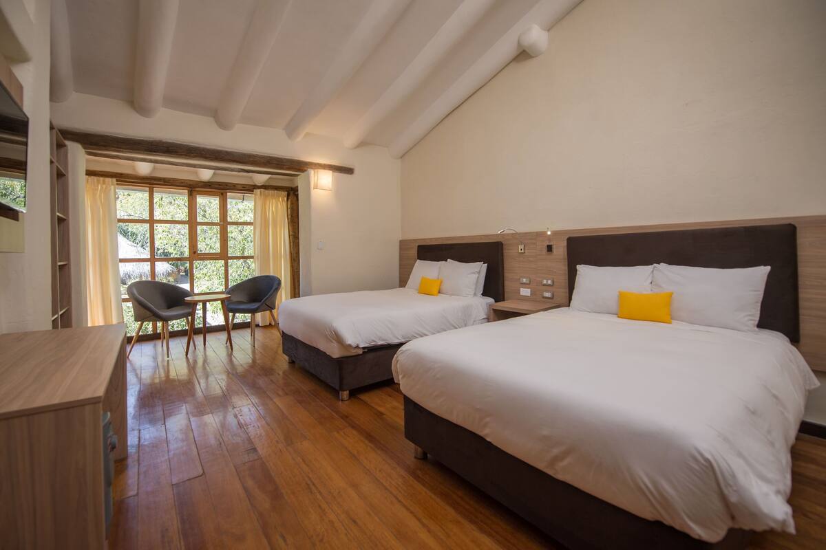 Quarto de hotel com duas camas, uma escrivaninha e uma cadeira.