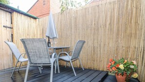 Um terraço com uma mesa e quatro cadeiras, cercado por uma cerca de bambu.