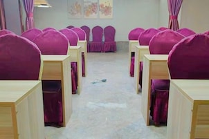 Um espaço com fileiras de cadeiras roxas e mesas de madeira, organizado como uma sala de aula.