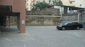 Área de estacionamento com um carro preto estacionado perto da entrada de um edifício.