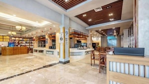 Um hall amplo com piso de mármore, balcão de recepção em madeira e área de café.