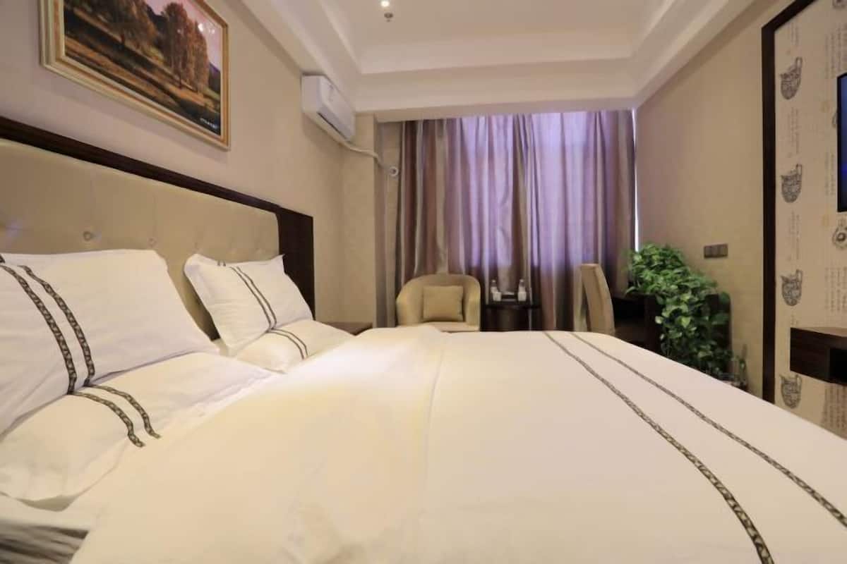 Quarto de hotel com uma cama grande, uma cadeira, uma escrivaninha e uma planta.