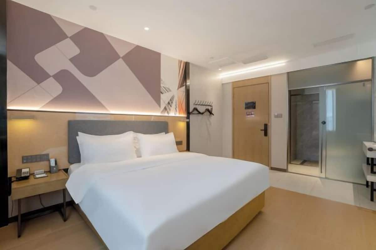 Quarto de hotel moderno com uma cama grande, uma mesa de cabeceira, TV fixada na parede e porta para o banheiro.