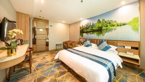 Quarto de hotel com uma cama grande, uma escrivaninha com cadeira, uma televisão e um quadro de uma paisagem na parede.